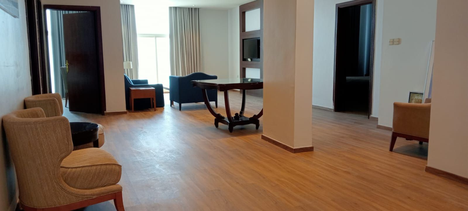 Uma sala de estar ampla com piso de madeira, uma mesa de jantar e várias cadeiras.