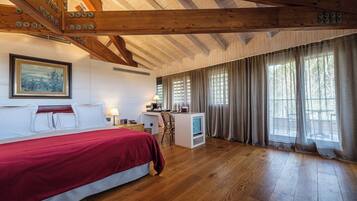 Quarto de hotel com teto de madeira, cama com colcha vermelha, escrivaninha com computador e janelas amplas com cortinas.