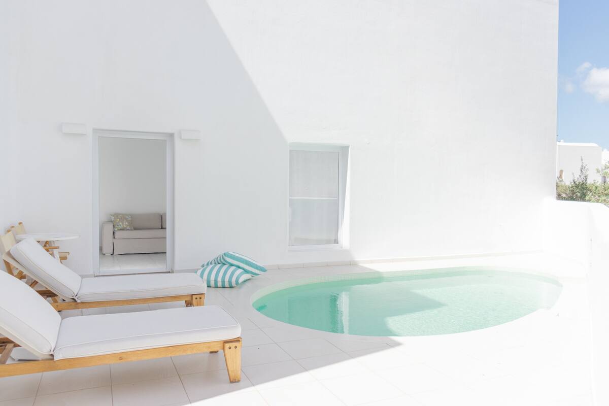 Um edifício moderno e branco com área de piscina, incluindo cadeiras de descanso e um pequeno espaço para sentar.