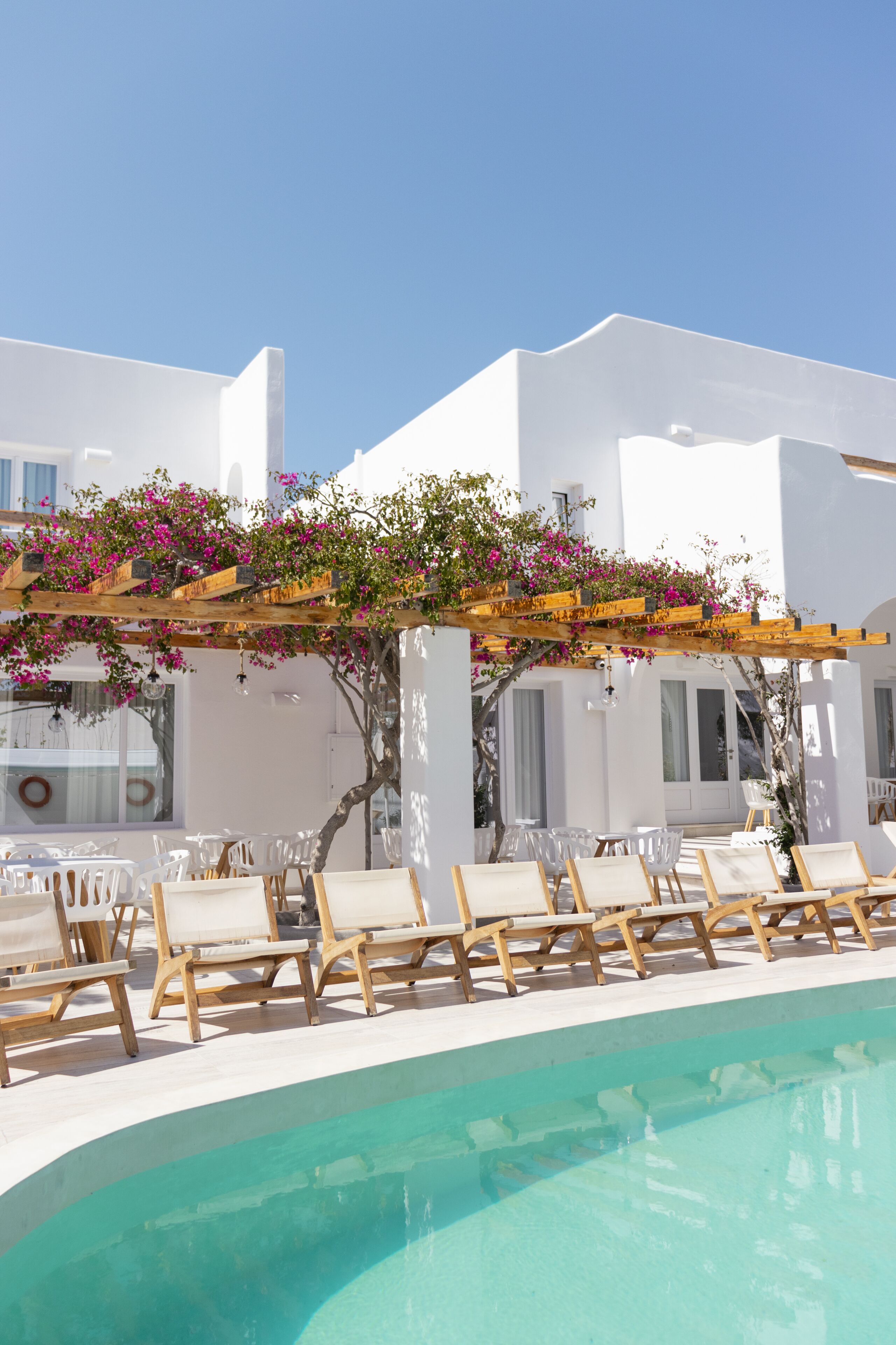Área de piscina com espreguiçadeiras e um pergolado coberto de plantas floridas.