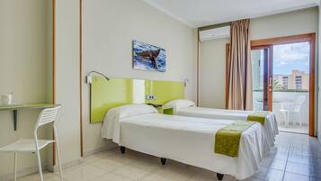 Quarto de hotel com duas camas, uma escrivaninha, uma cadeira e uma janela com vista para prédios.
