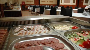 Uma área de buffet com diversas opções de comida, incluindo bacon, milho e uma salada.