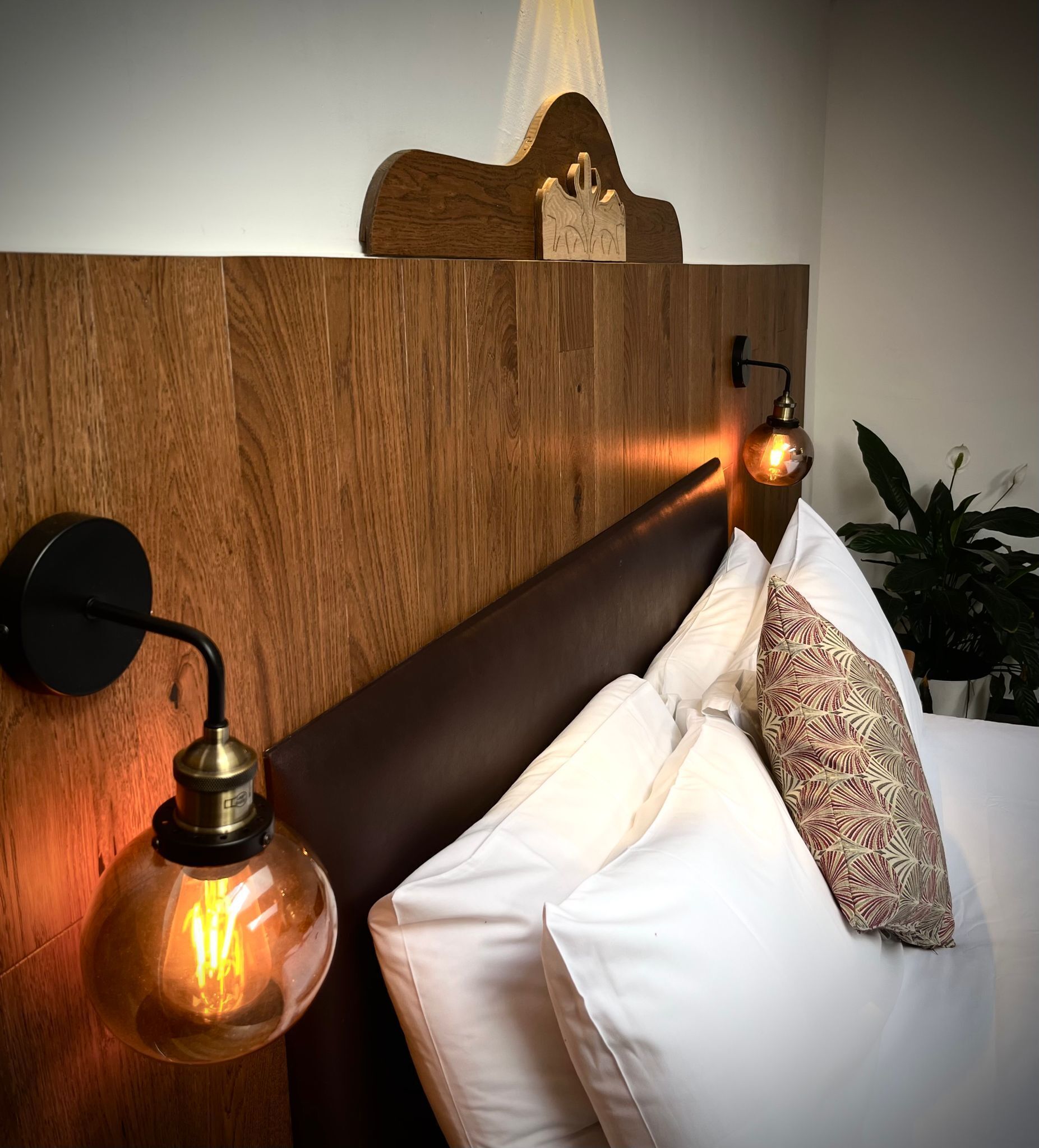 Quarto com cabeceira de madeira, luminária fixada na parede e cama com almofadas brancas e estampadas.