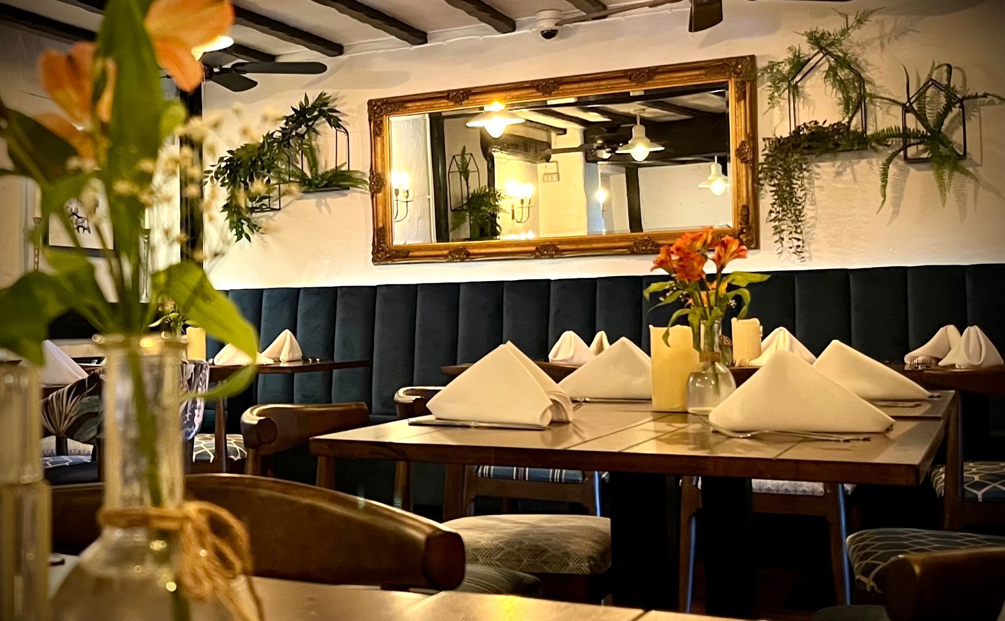 Restaurante com um banco estofado azul escuro, guardanapos brancos e um espelho sobre a mesa.