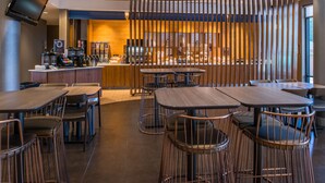 Um restaurante moderno com mesas e cadeiras de madeira, um balcão com uma máquina de café e uma televisão na parede.
