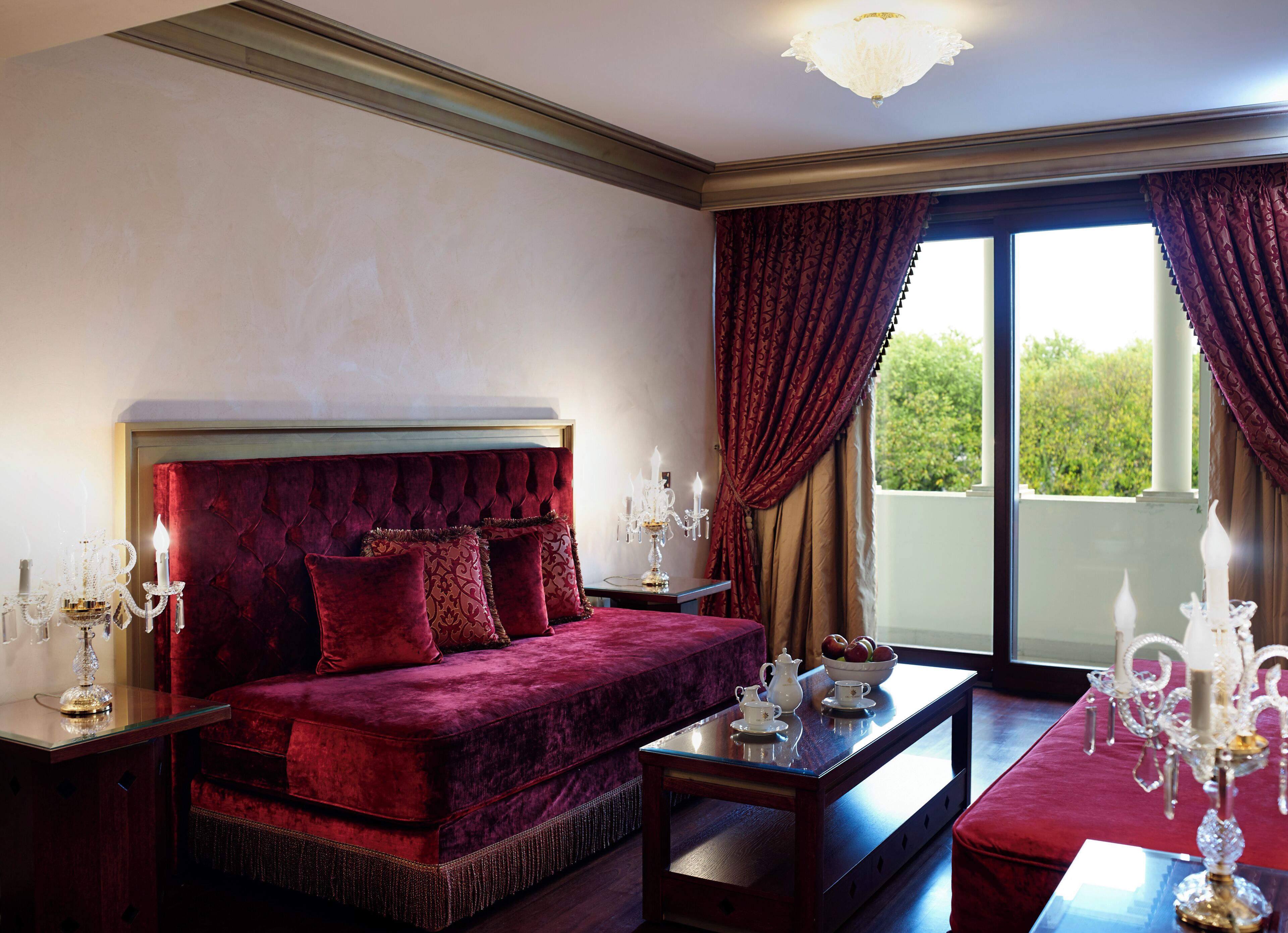 Um quarto com um sofá de veludo vermelho, uma mesa de centro de vidro e um candelabro.