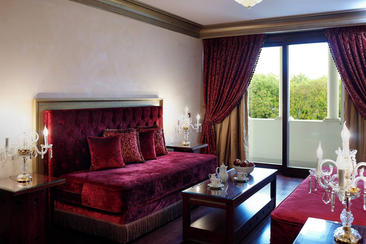 Um quarto com um sofá de veludo vermelho, uma mesa de centro de vidro e um candelabro.