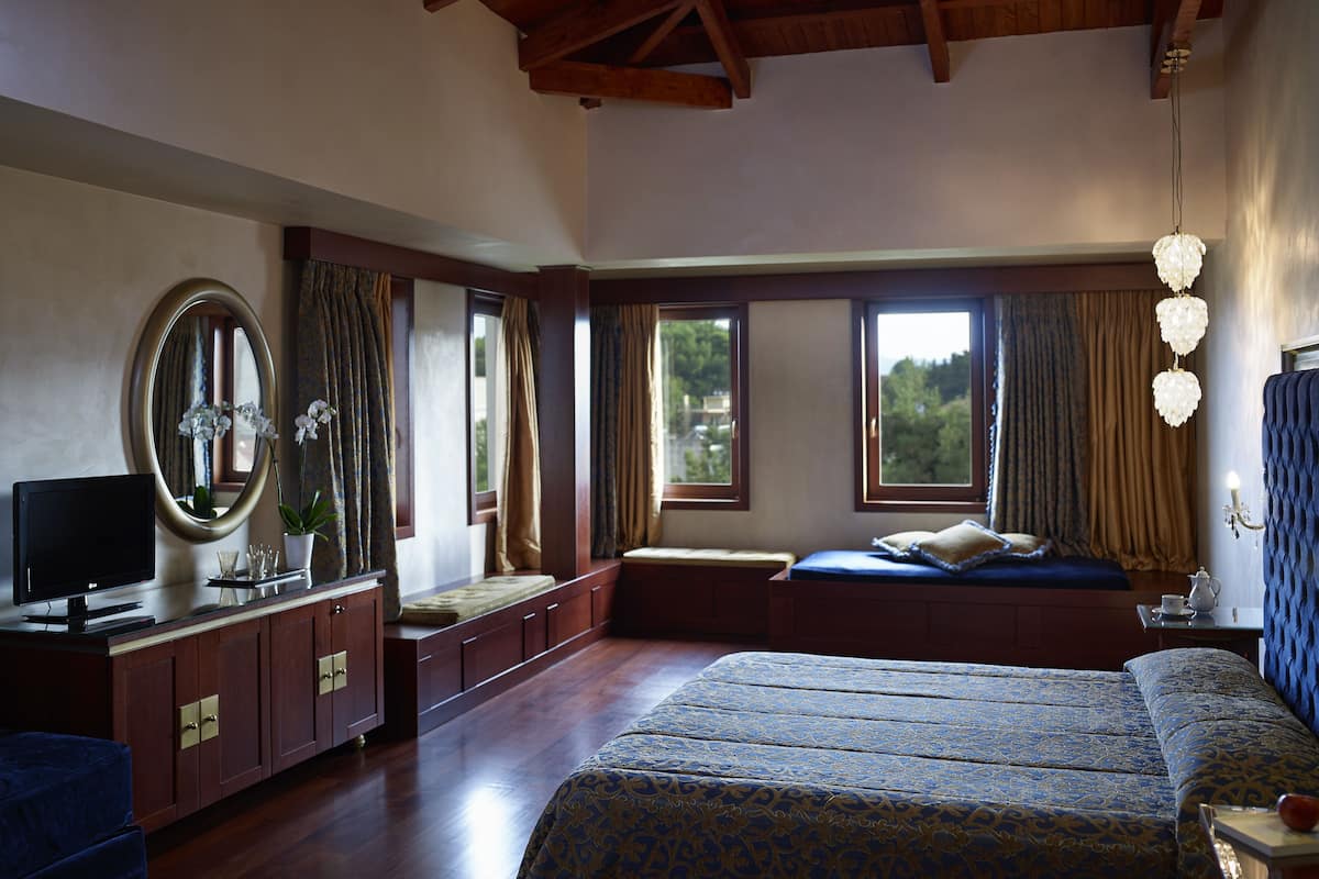 Quarto com cama grande, televisão, penteadeira e janela com cortinas.