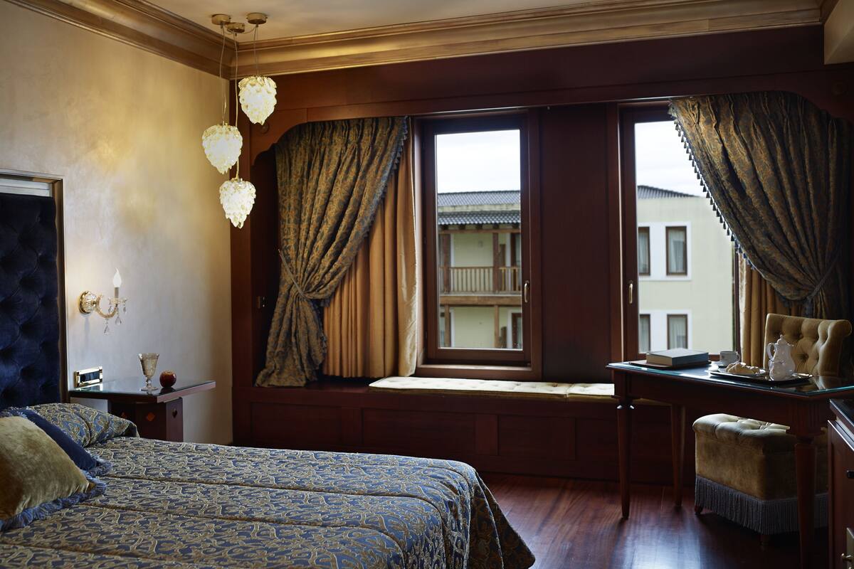 Quarto com cama grande, escrivaninha e janela com cortinas.