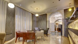 Um lobby de hotel moderno com piso de mármore, área de estar com poltronas de couro e balcão de recepção.