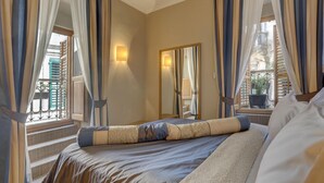 Quarto de hotel com uma cama grande, um espelho e cortinas. Há uma janela com vista para uma varanda.