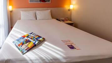 Quarto de hotel com cama, mesa de cabeceira, ar condicionado fixado na parede e um quadro emoldurado sobre a cama.