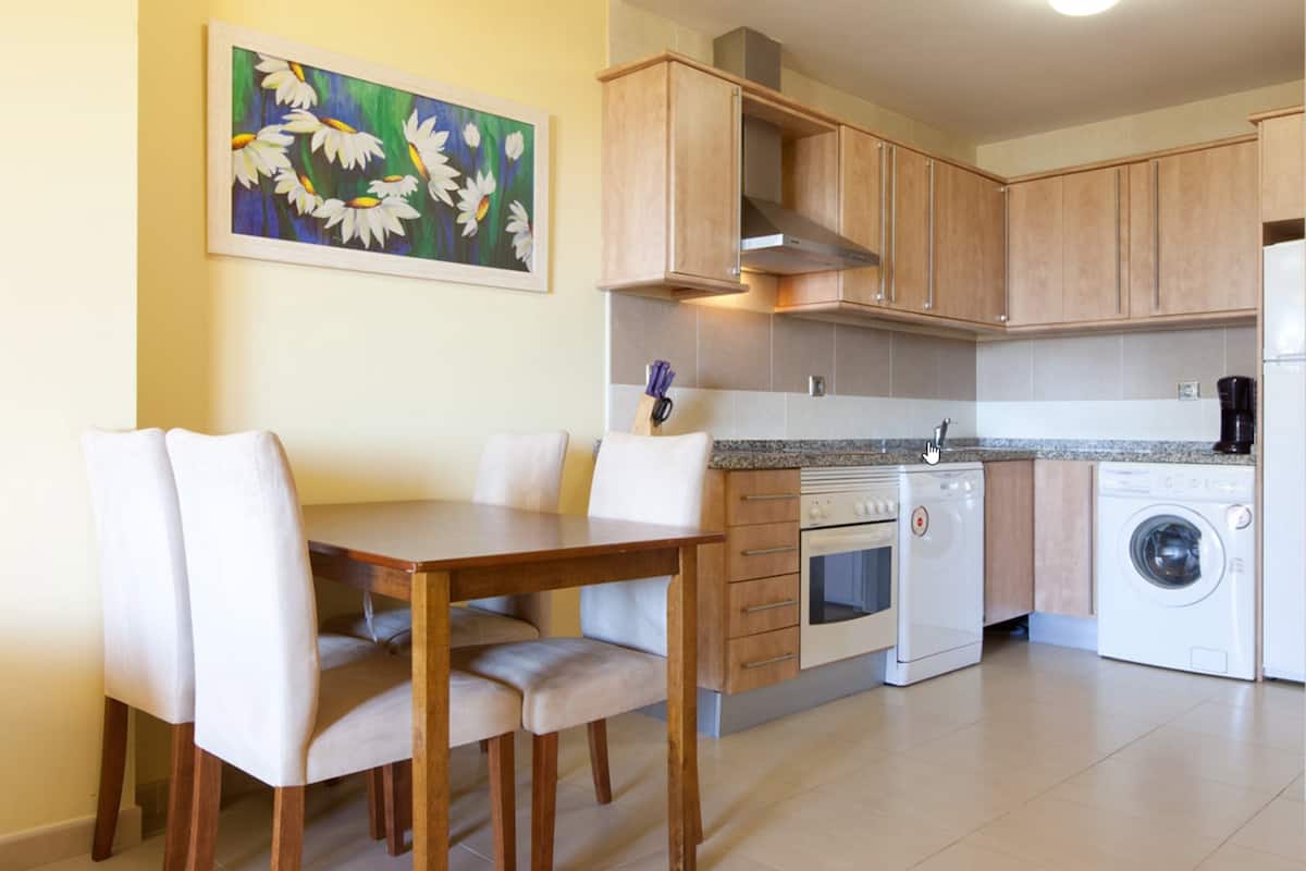 Uma cozinha moderna com armários de madeira, forno embutido, máquina de lavar e área de jantar com mesa e cadeiras.