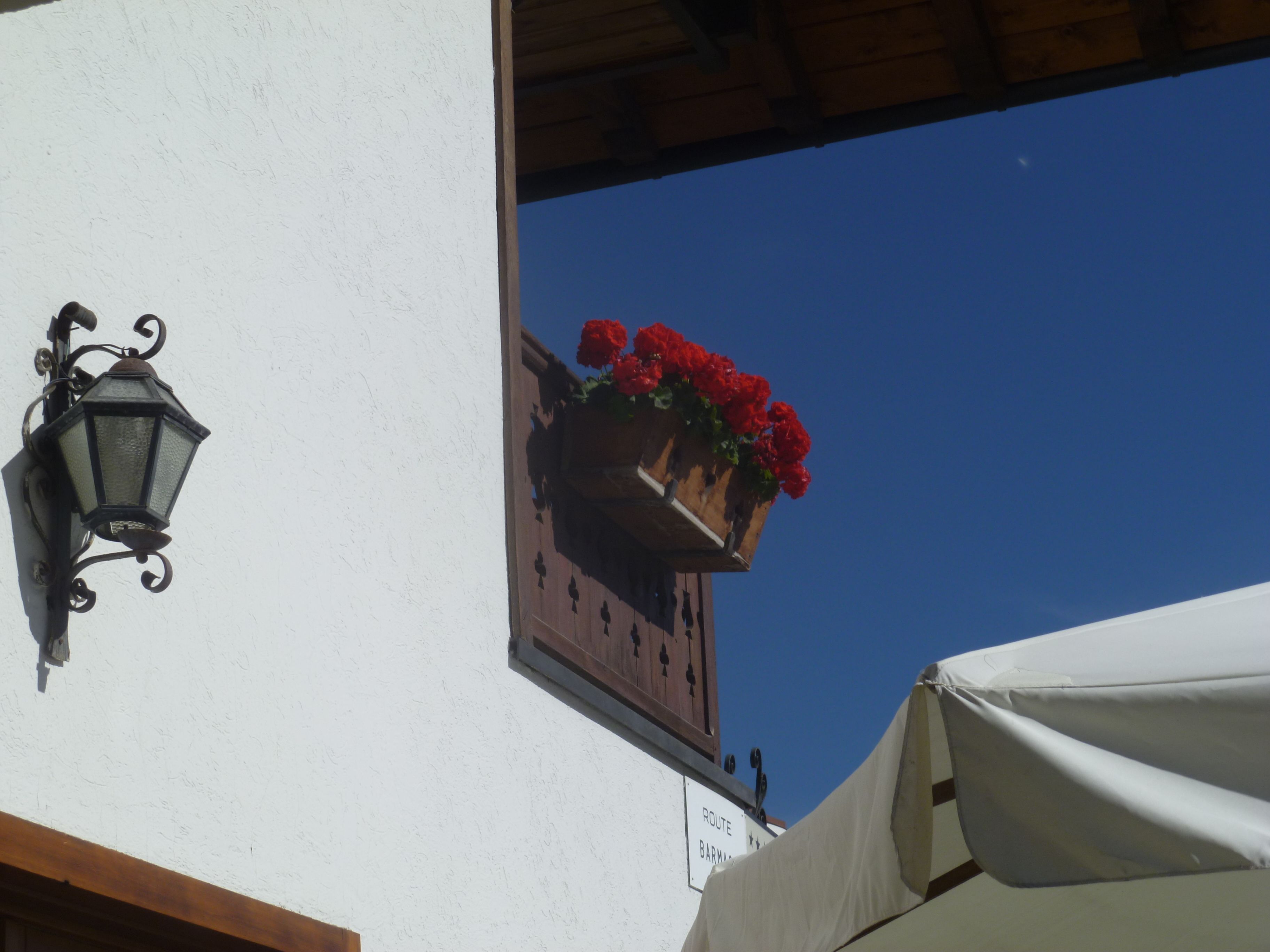Um edifício com fachada branca, um lampião de metal preto e uma cesta de flores com flores vermelhas.