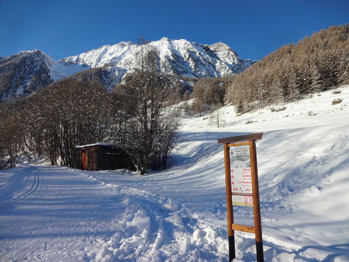 Uma trilha coberta de neve na montanha com um sinal de madeira indicando direções para vários locais.