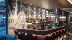 Uma área de bar moderna com um balcão comprido, banquetas e diversos tipos de garrafas e copos.