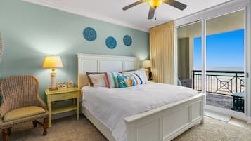 Quarto com cama, cadeira, mesa de cabeceira, ventilador de teto e vista da praia através de uma porta de correr.