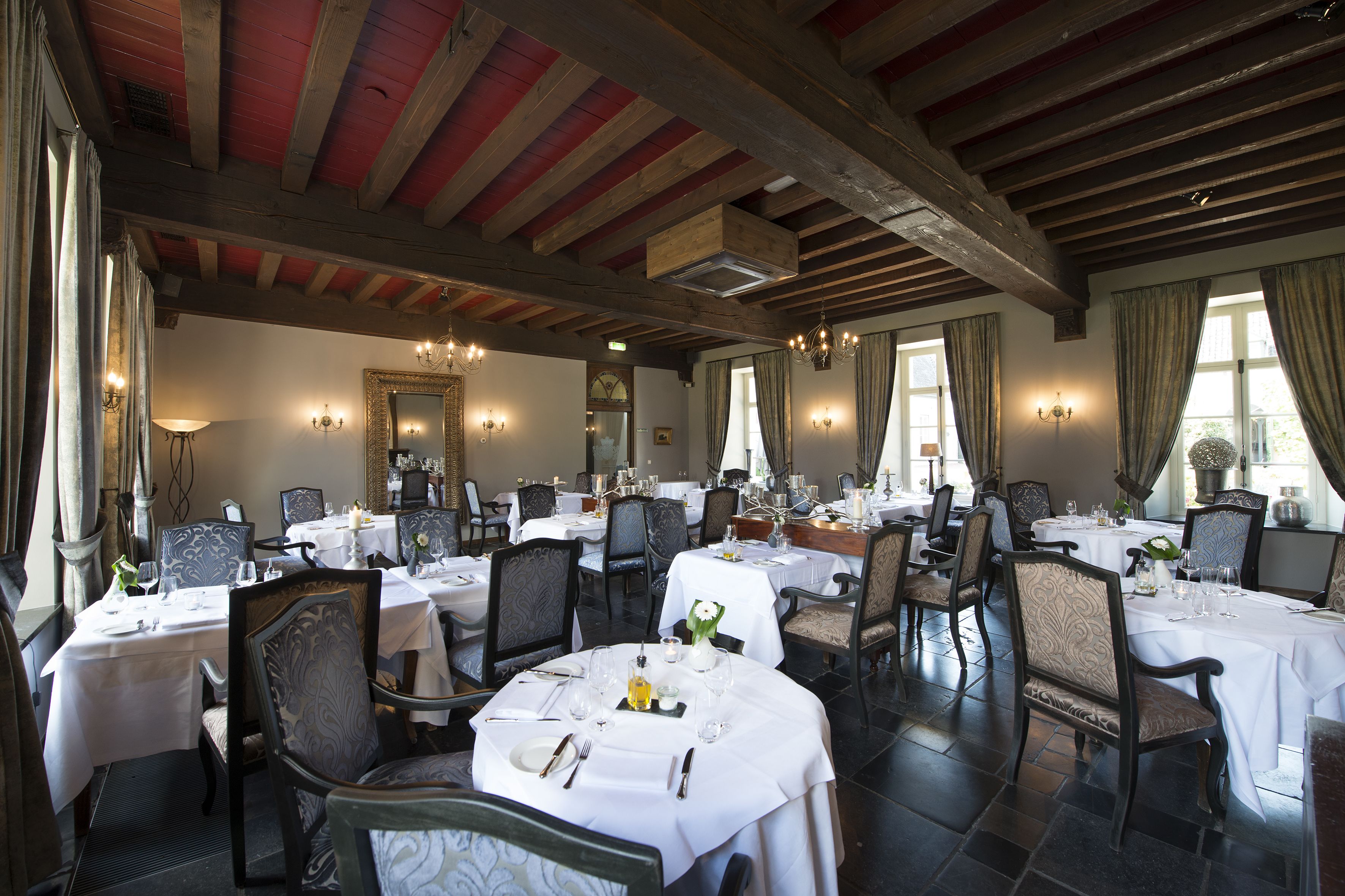 Uma sala de jantar com várias mesas preparadas para hóspedes, com vigas de madeira clássicas e lustres.