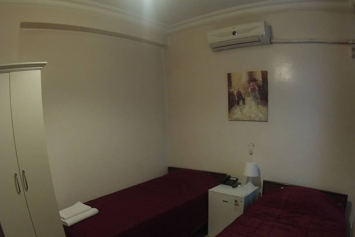 Quarto com duas camas de solteiro, um guarda-roupa, mesa de cabeceira com abajur e um aparelho de ar condicionado na parede.