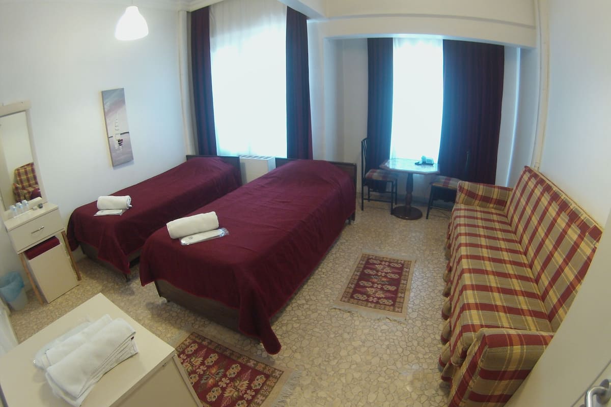 Quarto de hotel com duas camas, uma escrivaninha, um sofá, banheiro e uma janela com cortinas.