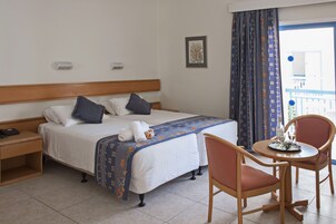 Quarto de hotel com cama, mesa de cabeceira, cadeira e uma pequena mesa com garrafa e copo.