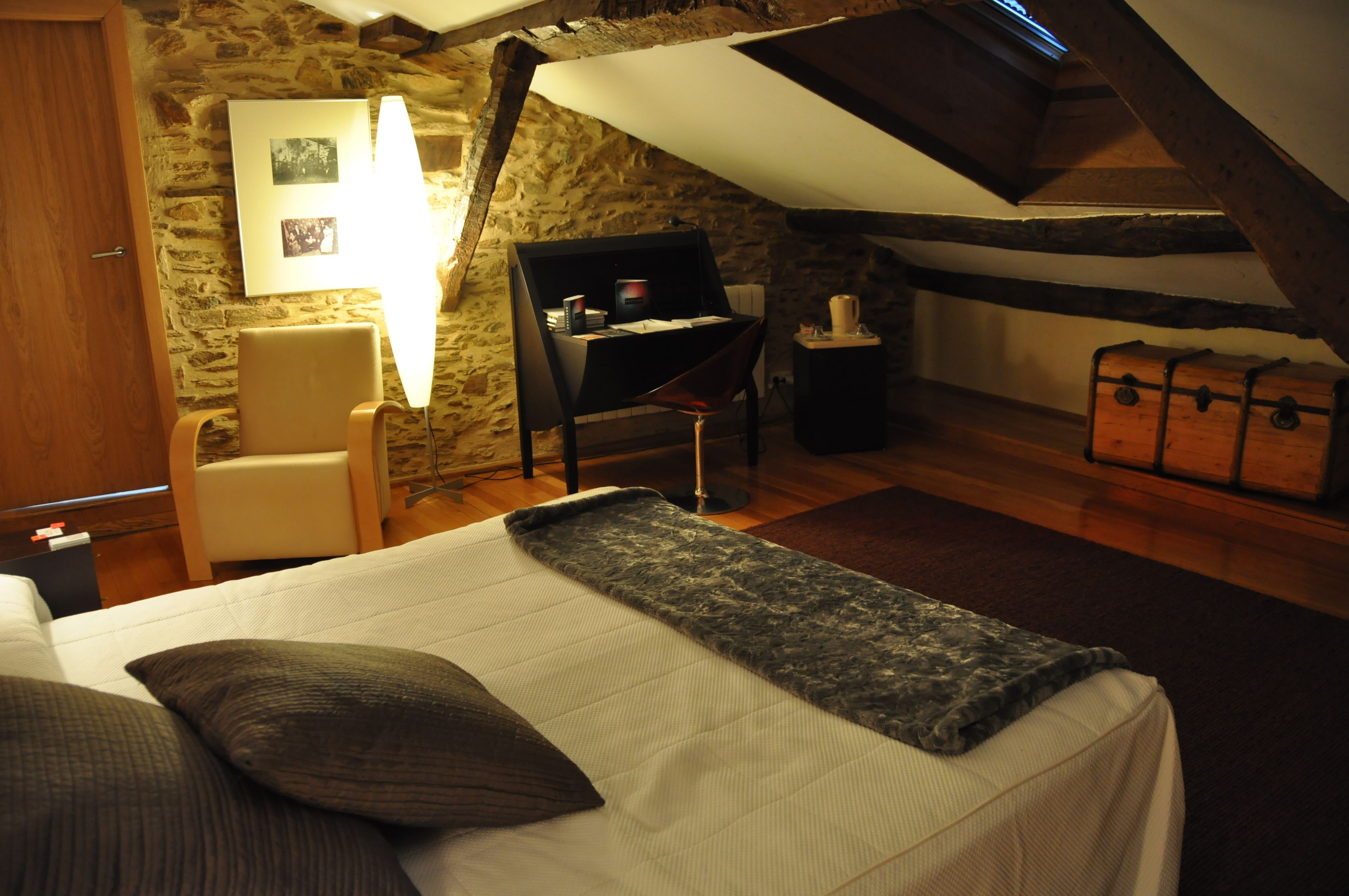 Um quarto de sótão aconchegante com cama, cadeira, escrivaninha e mala.