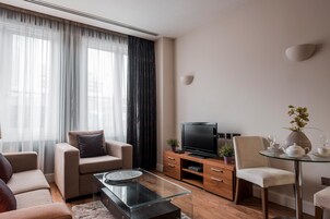 Uma sala de estar moderna com um sofá, uma mesa de centro de vidro, uma televisão e uma área de jantar com mesa e cadeiras de vidro.