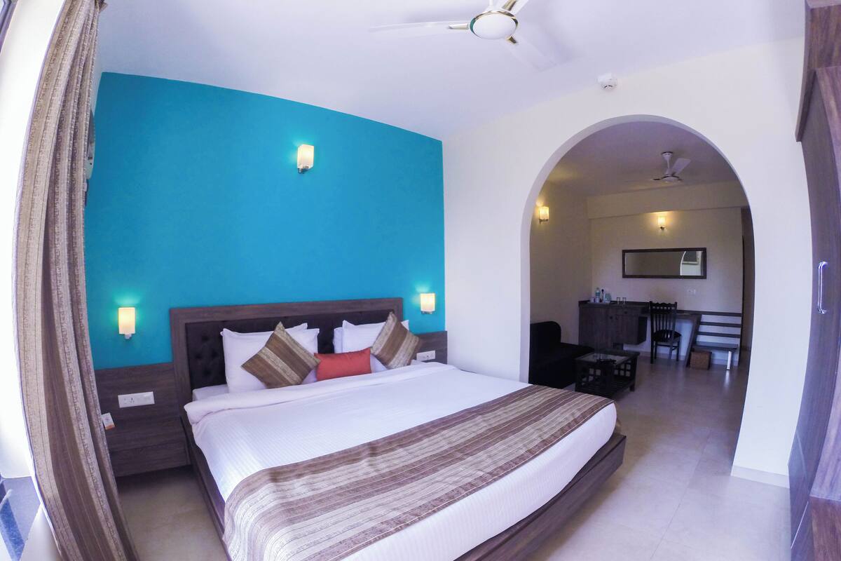 Quarto de hotel com uma cama grande, duas mesas de cabeceira, uma escrivaninha e uma cadeira.