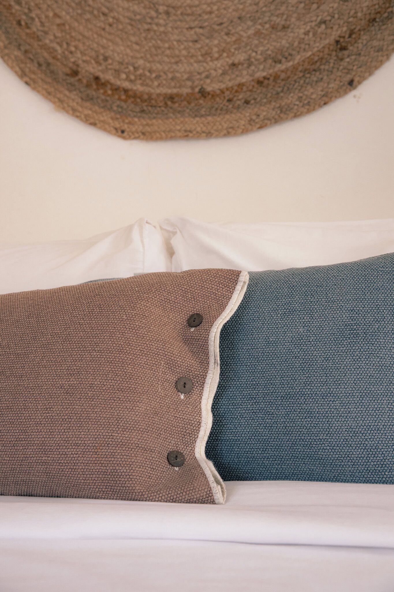 Cama com duas almofadas, uma marrom e outra azul, e cabeceira trançada acima.