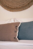 Cama com duas almofadas, uma marrom e outra azul, e cabeceira trançada acima.