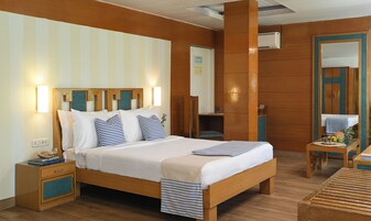 Quarto de hotel bem arrumado com cama de madeira, almofadas listradas, mesa de cabeceira com abajur e espelho.