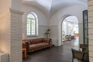 Um quarto amplo com sofá de couro, cadeiras de vime e paredes de tijolos brancos.