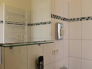 Casa de banho com divisória de vidro, secador de mãos e dispensador de toalhas.