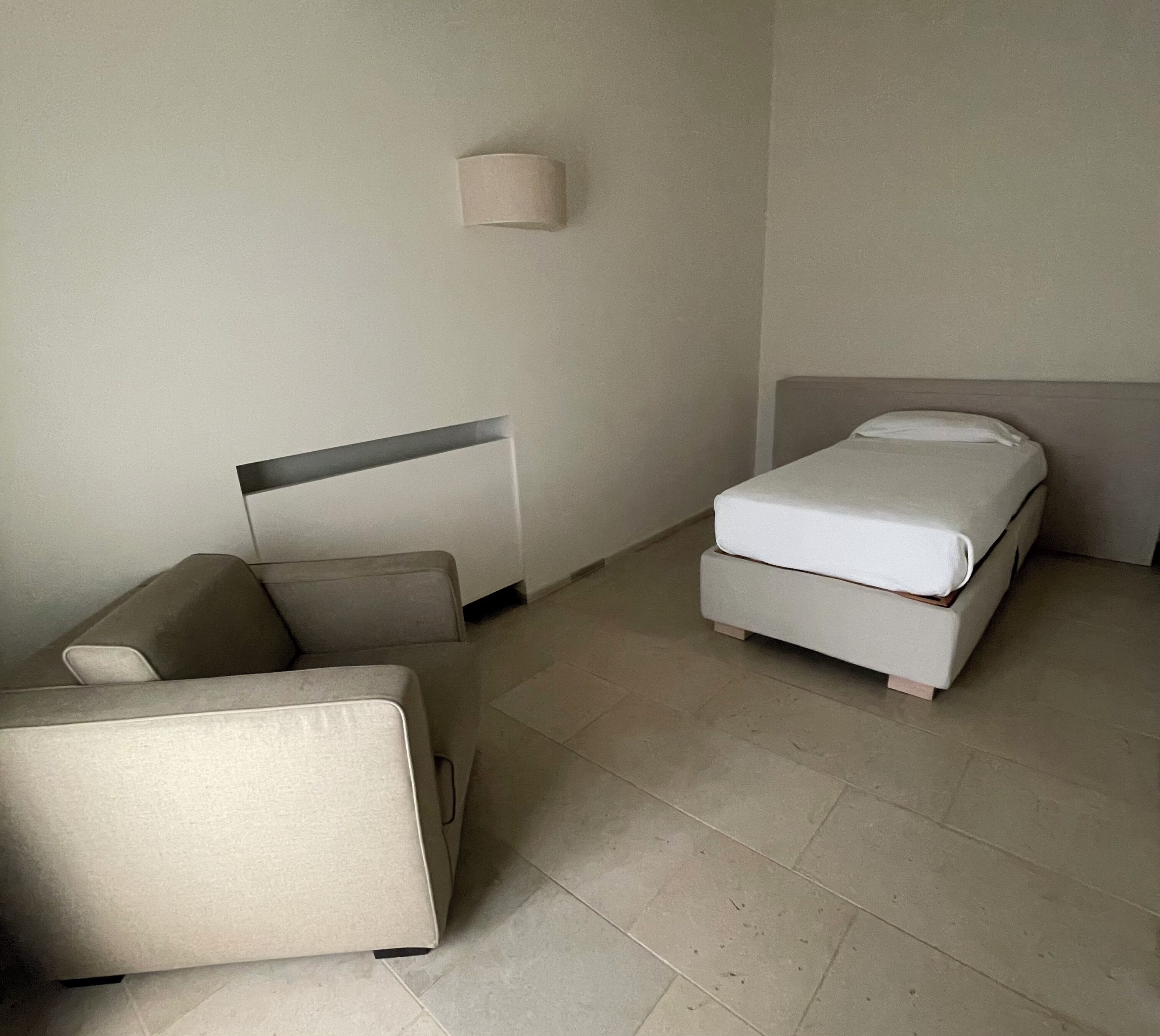 Quarto de hotel com uma cama, um sofá e uma luminária fixada na parede.