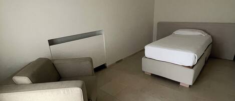 Quarto de hotel com uma cama, um sofá e uma luminária fixada na parede.