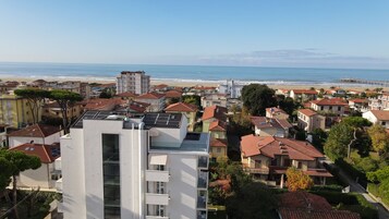 Uma área residencial costeira com edifícios de telhado vermelho, alguns com painéis solares, e vista para a praia e oceano.