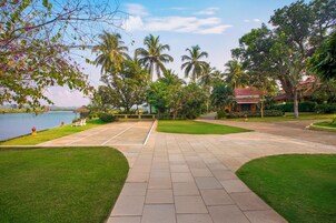 Uma trilha pavimentada leva a um edifício com vista para um lago e palmeiras.