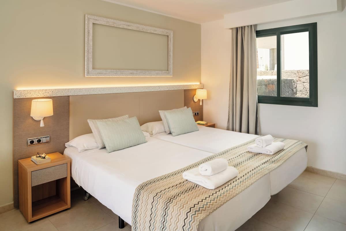 Uma cama de casal com manta estampada, luminárias de cabeceira, mesa de cabeceira e um quadro na parede.