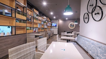 Interior de restaurante com móveis de vime, prateleiras de madeira e um relógio de parede.