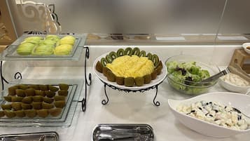Buffet com diversos alimentos, incluindo frutas fatiadas, um bolo e saladas.