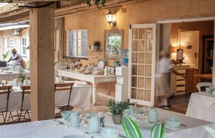 Uma sala de jantar com mesas postas para refeição, com louças azul claro e um vaso de planta central.
