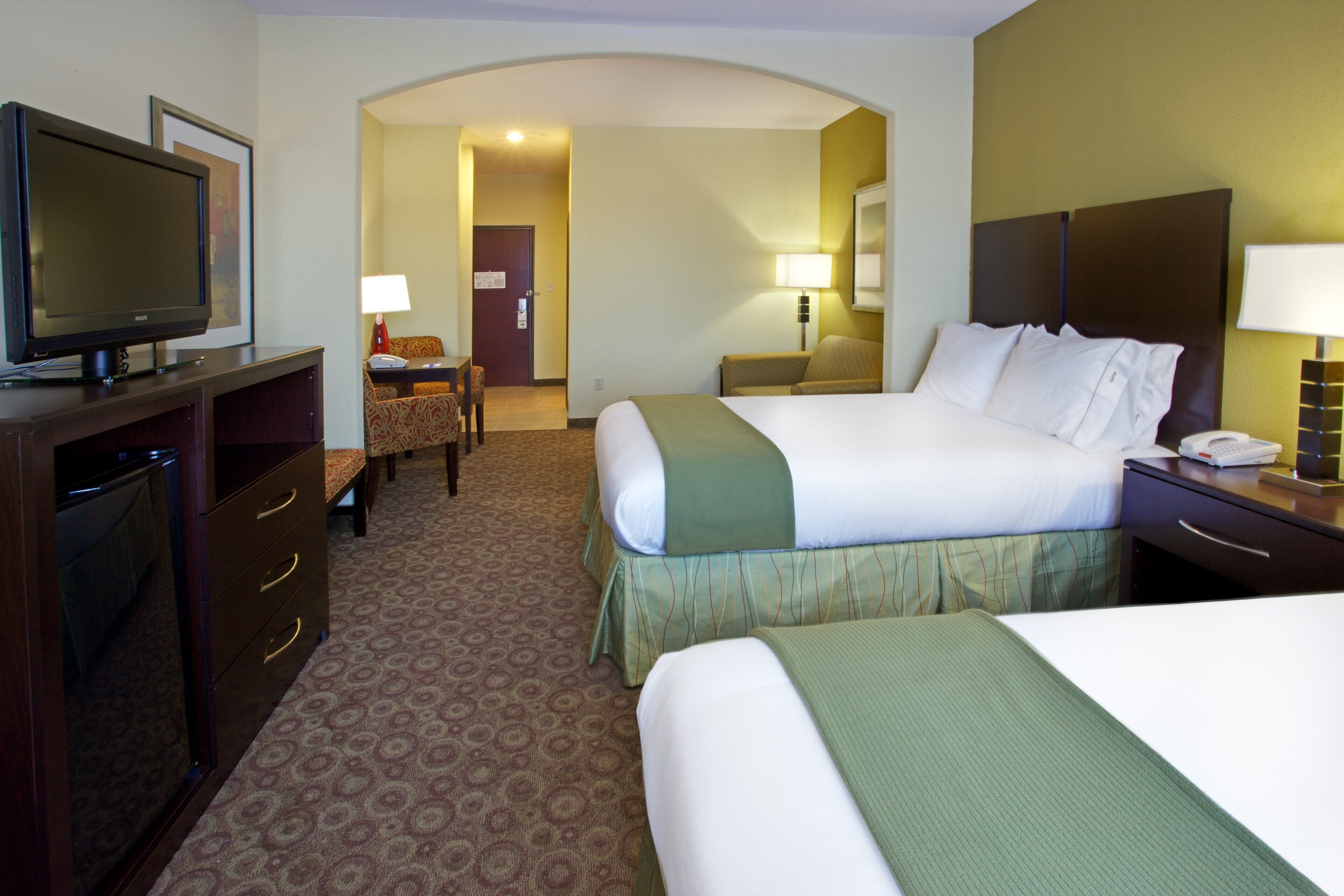 Quarto de hotel com cama, escrivaninha, televisão e cadeira.