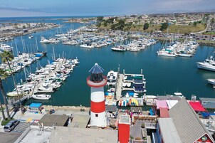 Uma marina com vários barcos atracados, um farol imponente e vista da cidade ao redor.