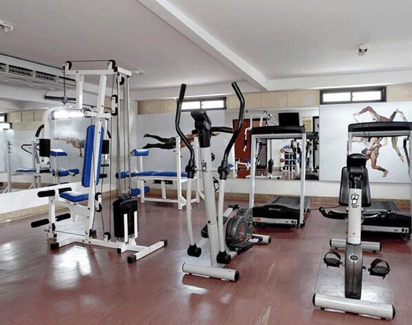 Uma academia com diversos equipamentos de exercício, esteira e um espelho grande na parede.
