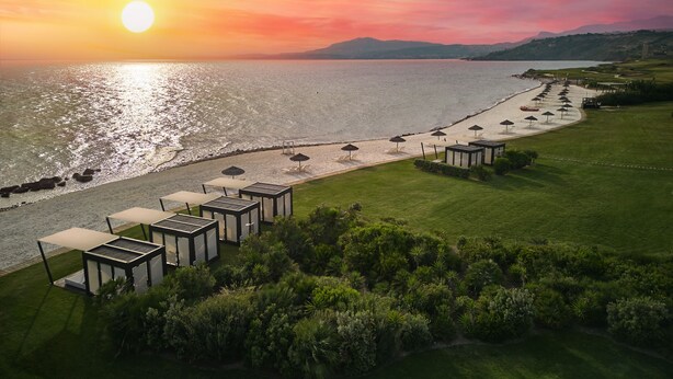 Um resort à beira-mar com praia, espreguiçadeiras e vista para o pôr do sol no oceano.