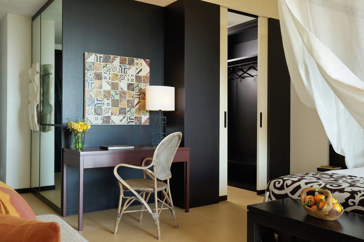 Quarto de hotel com escrivaninha, cadeira, cama e guarda-roupa.