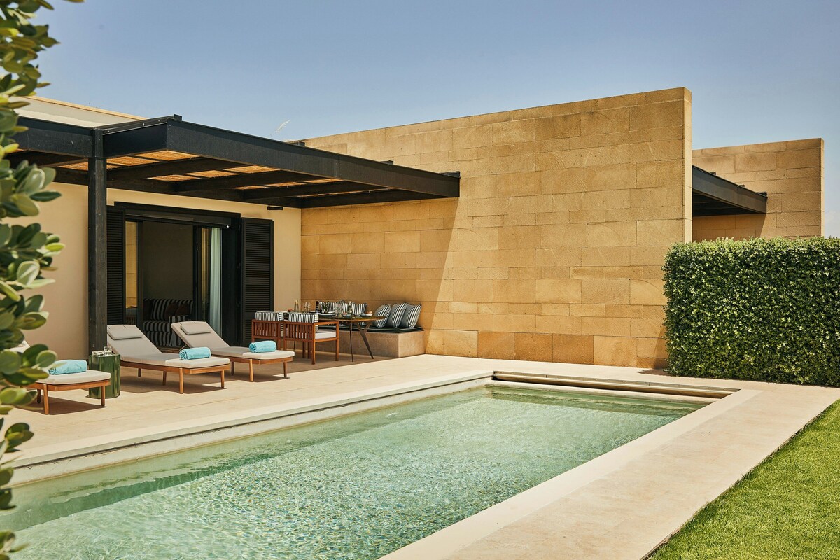 Uma área à beira da piscina com um espaço de estar coberto, uma mesa e cadeiras.