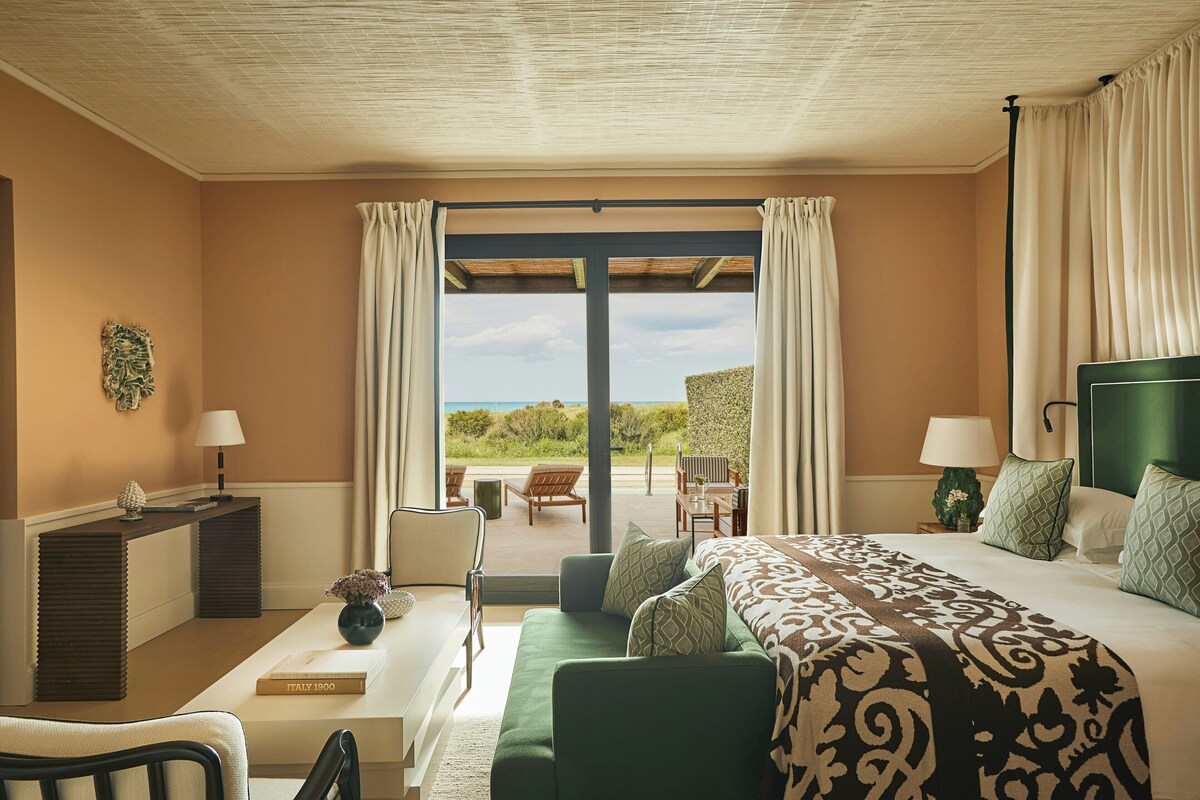 Quarto de hotel com cama, escrivaninha, poltrona, sofá e vista para o exterior.