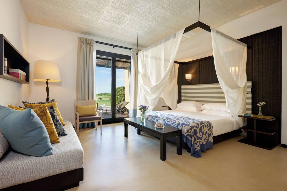 Quarto com cama de dossel, sofá, mesa de cabeceira e vista para o exterior.