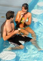 Duas pessoas sentadas em uma piscina, uma delas segurando um copo de cerveja.